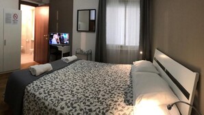 Quarto de hotel com cama, escrivaninha, televisão e guarda-roupa.