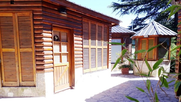 Uma cabana de toras com um pátio de pedras, venezianas de madeira e uma pequena área de jardim.
