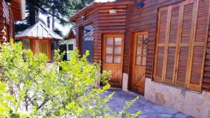 Uma cabana de madeira com um pátio calçado em pedra e um pequeno jardim com arbustos verdes.
