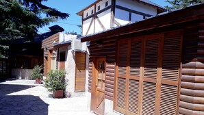 Uma cabana de madeira tradicional com alicerce de pedra, venezianas de madeira e um pátio pavimentado em pedra.