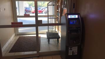Entrada com porta deslizante automática, aviso de segurança para manter distância, tapete e um caixa eletrônico.