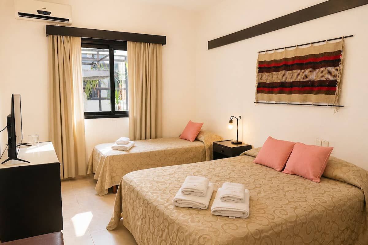 Quarto de hotel com duas camas, uma mesa, uma televisão e uma janela com cortinas.