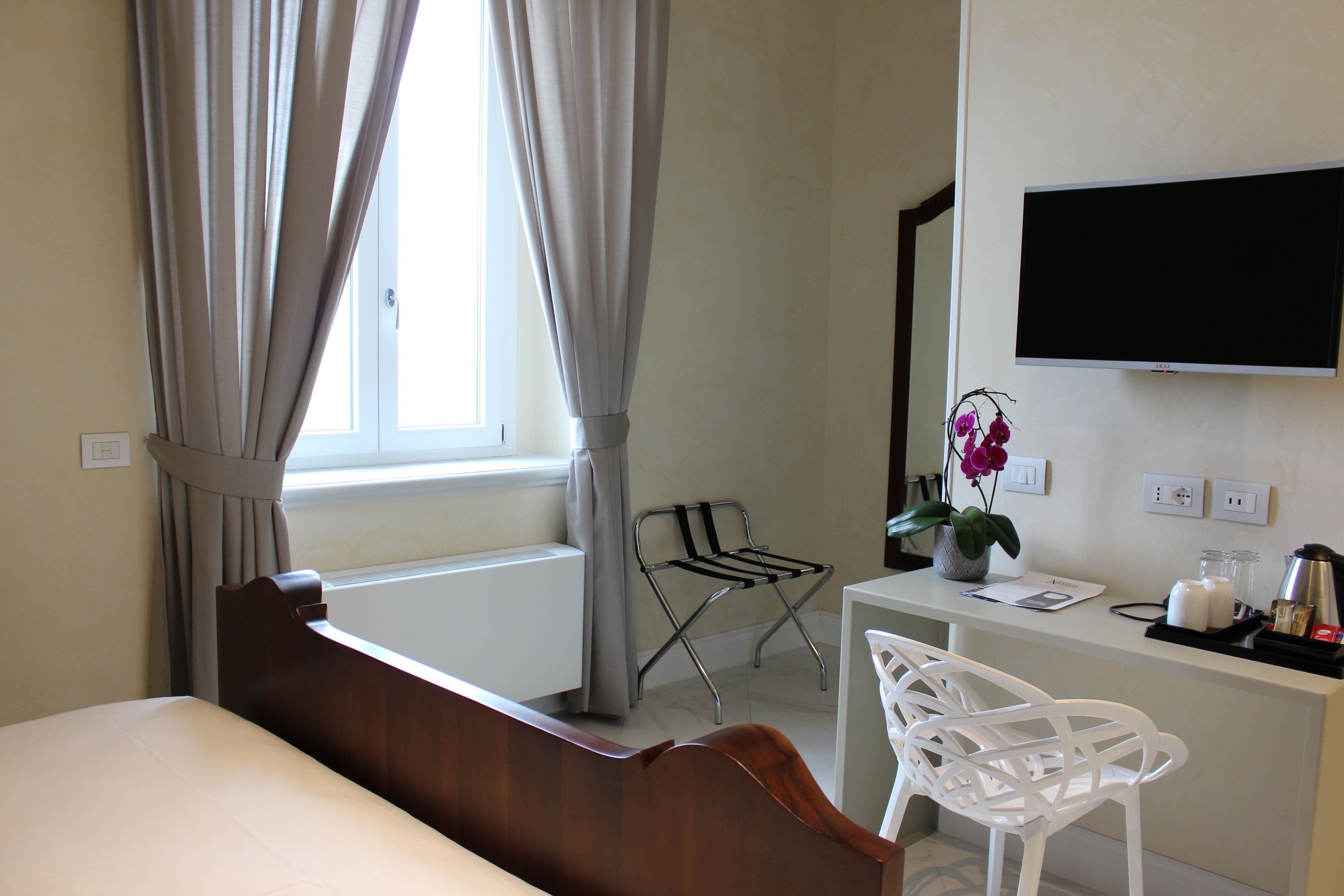 Quarto de hotel com cama, escrivaninha com cadeira, televisão e janela com cortinas.