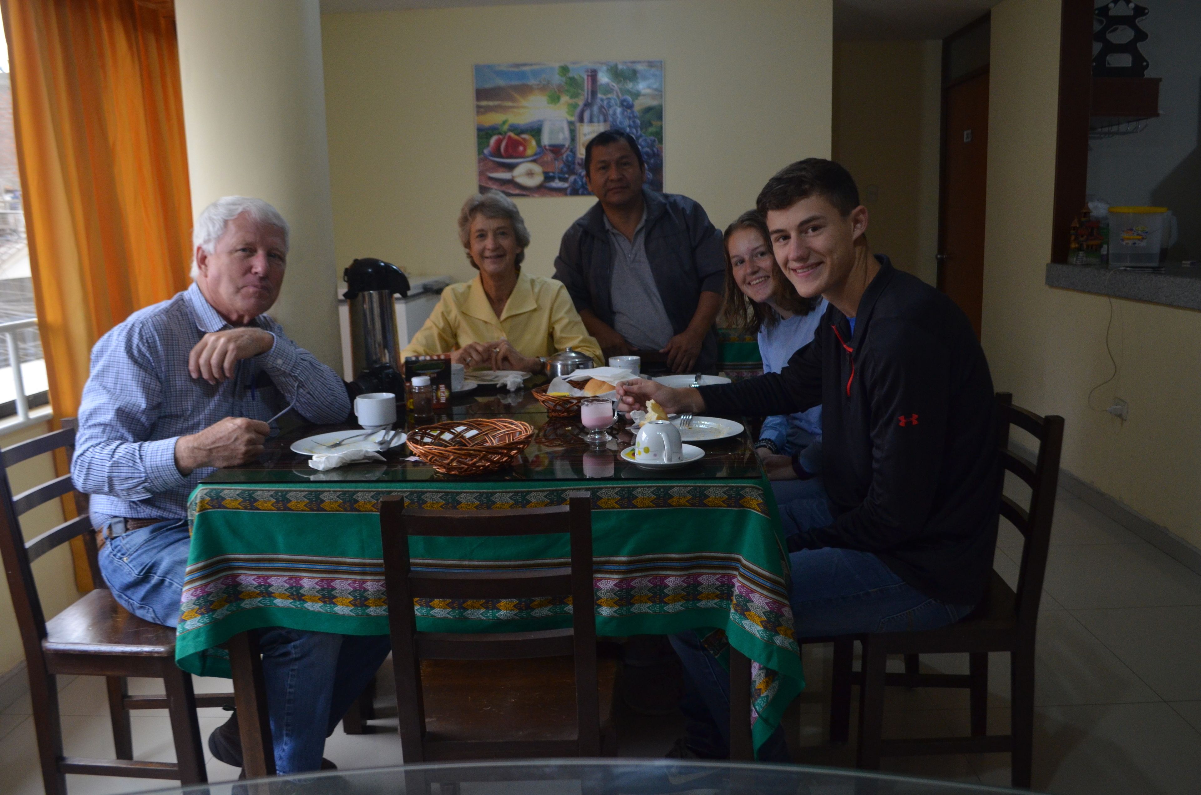 Uma mesa de jantar com toalha verde, rodeada por cadeiras de madeira.