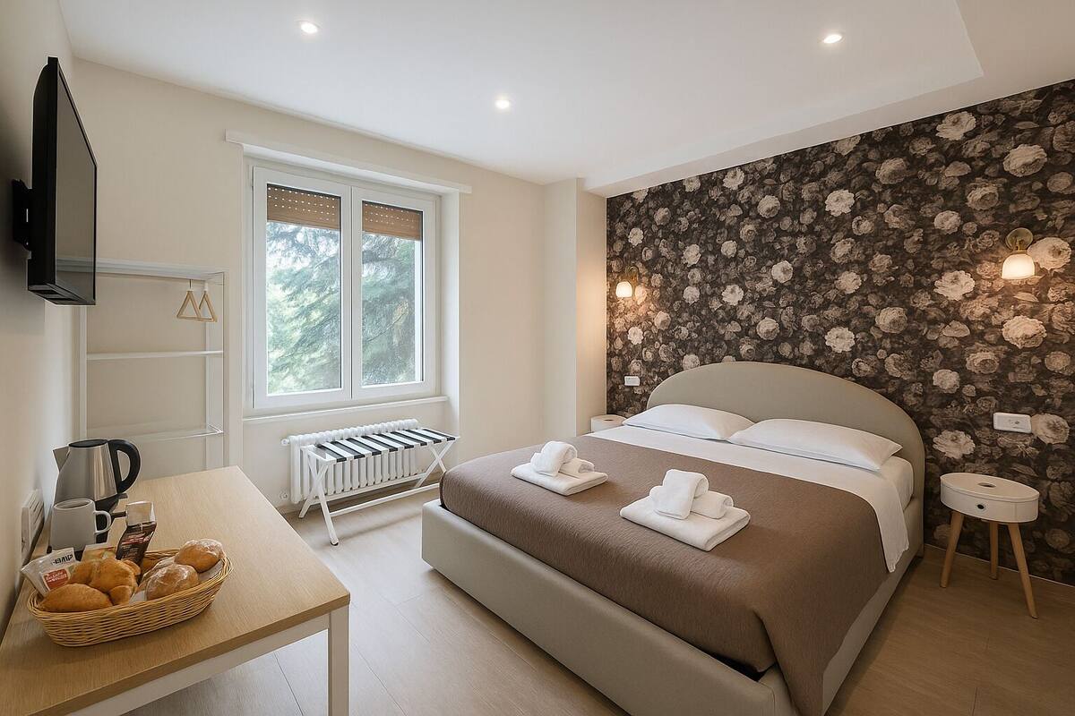 Quarto com cama, radiador, janela, mesa com cesta de pão e parede com padrão floral.