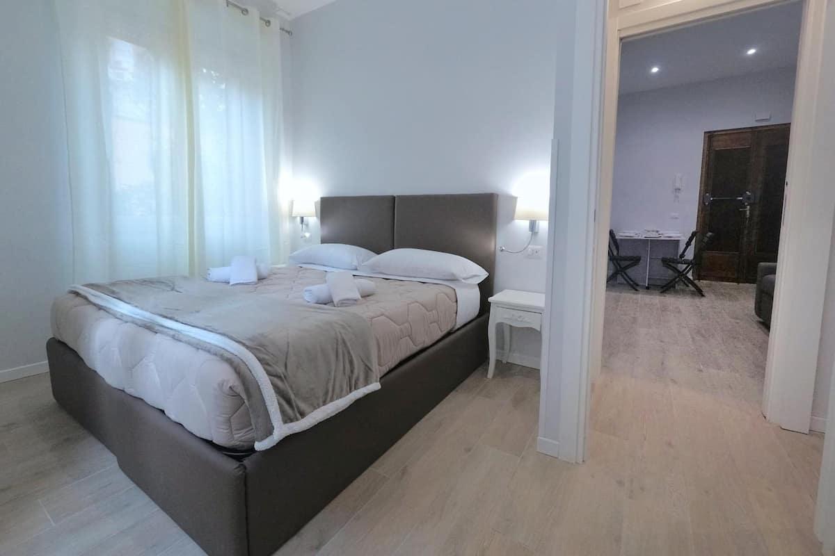 Quarto moderno com uma cama grande, mesas de cabeceira e uma área de escritório.