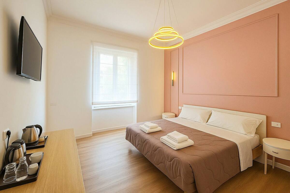 Quarto de hotel com cama, mesas de cabeceira, televisão, janela e luminária moderna.