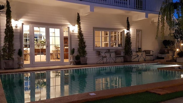 Área de piscina com piscina transparente, plantas em vasos e mobiliário de exterior.