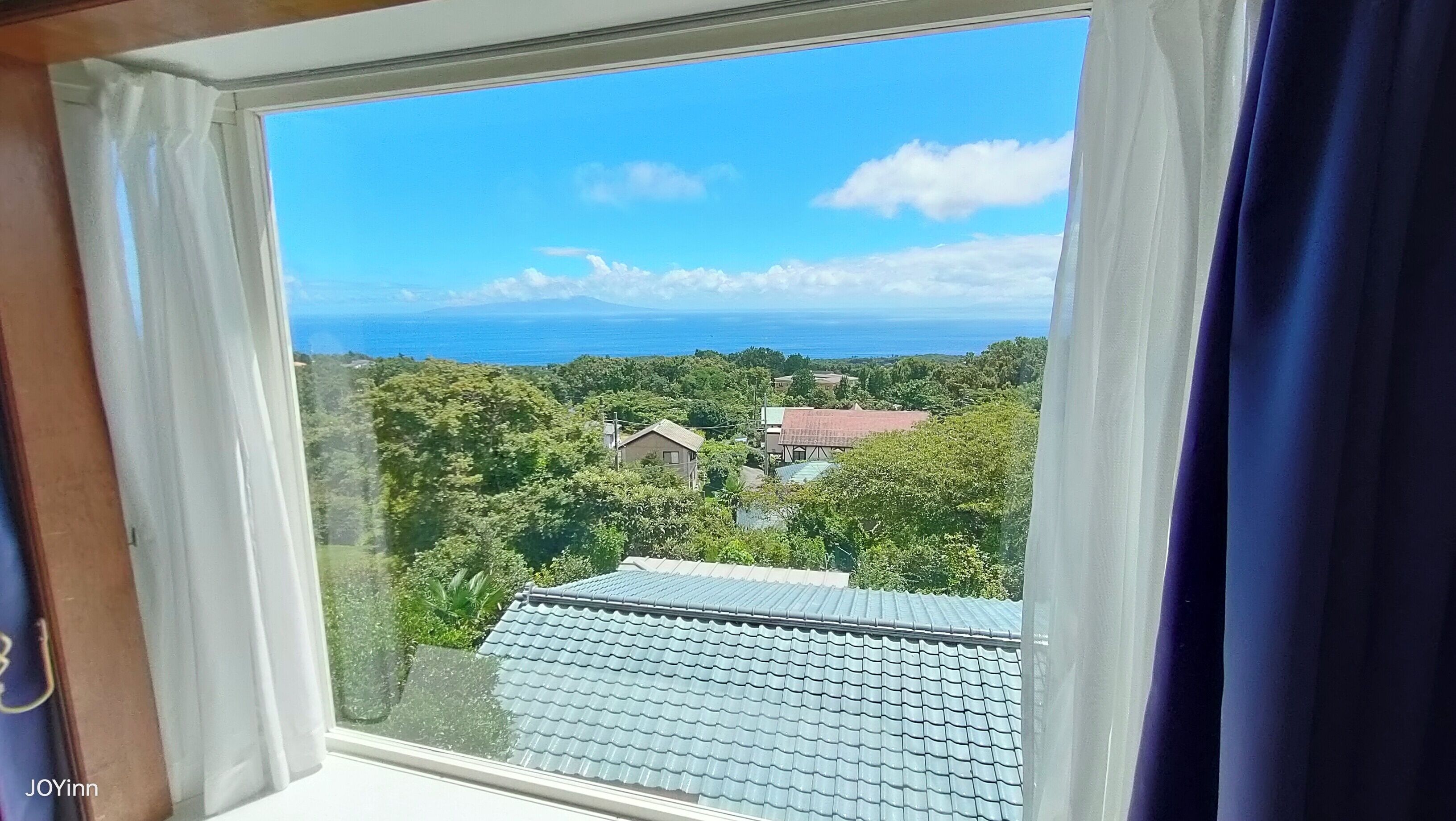 Vista da janela para uma área costeira com casas e vegetação.