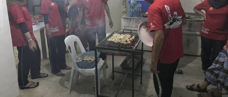 Um grupo de pessoas em uma cozinha com uma churrasqueira e uma cadeira de plástico branca.