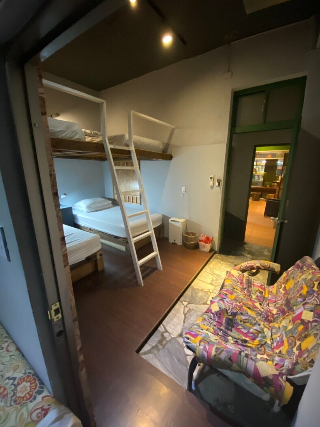 Quarto pequeno com beliche, escada, mesa compacta e um sofá colorido.