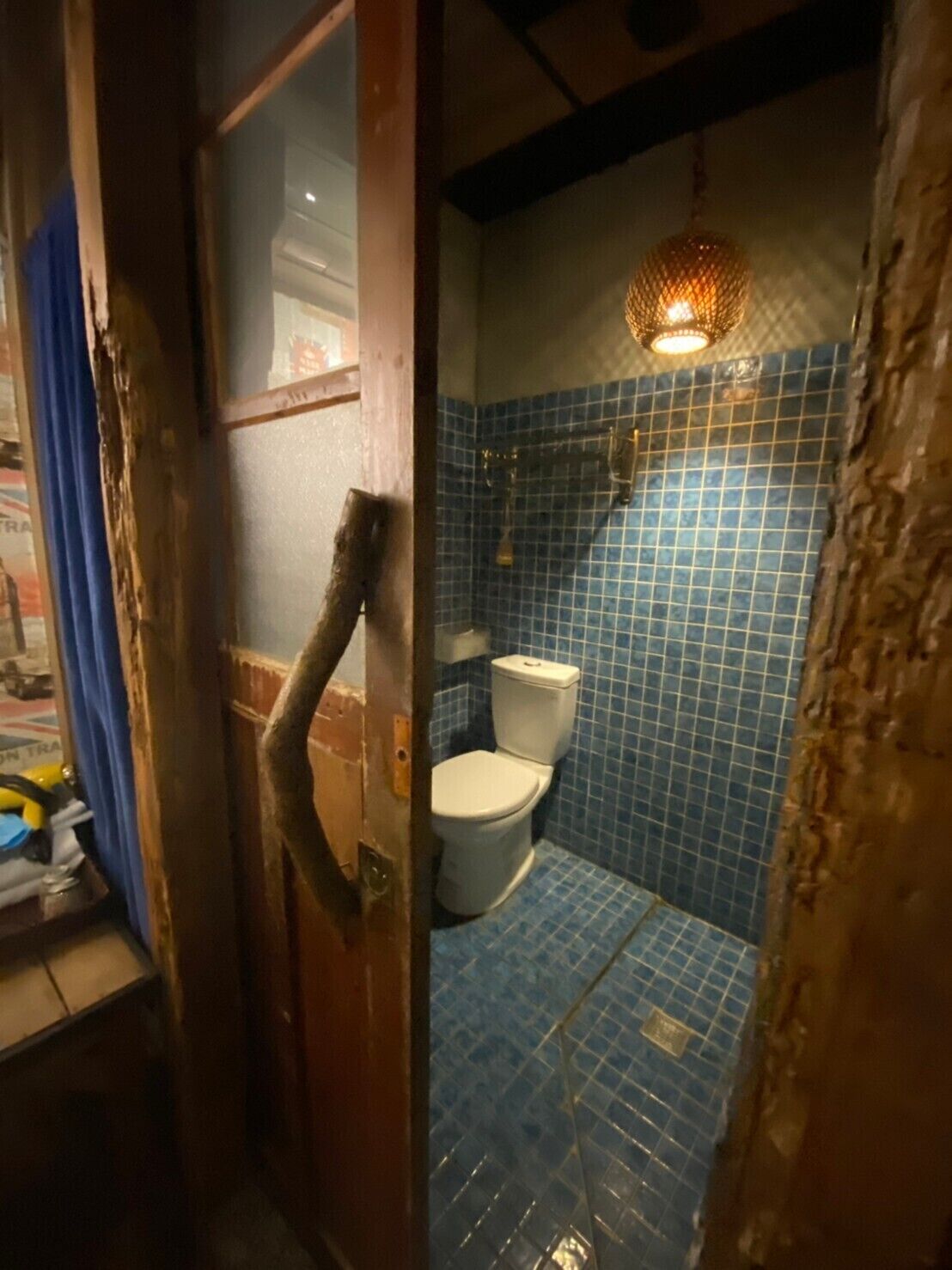 Casa de banho com chão e paredes azulejadas em azul, sanita branca e candeeiro suspenso.