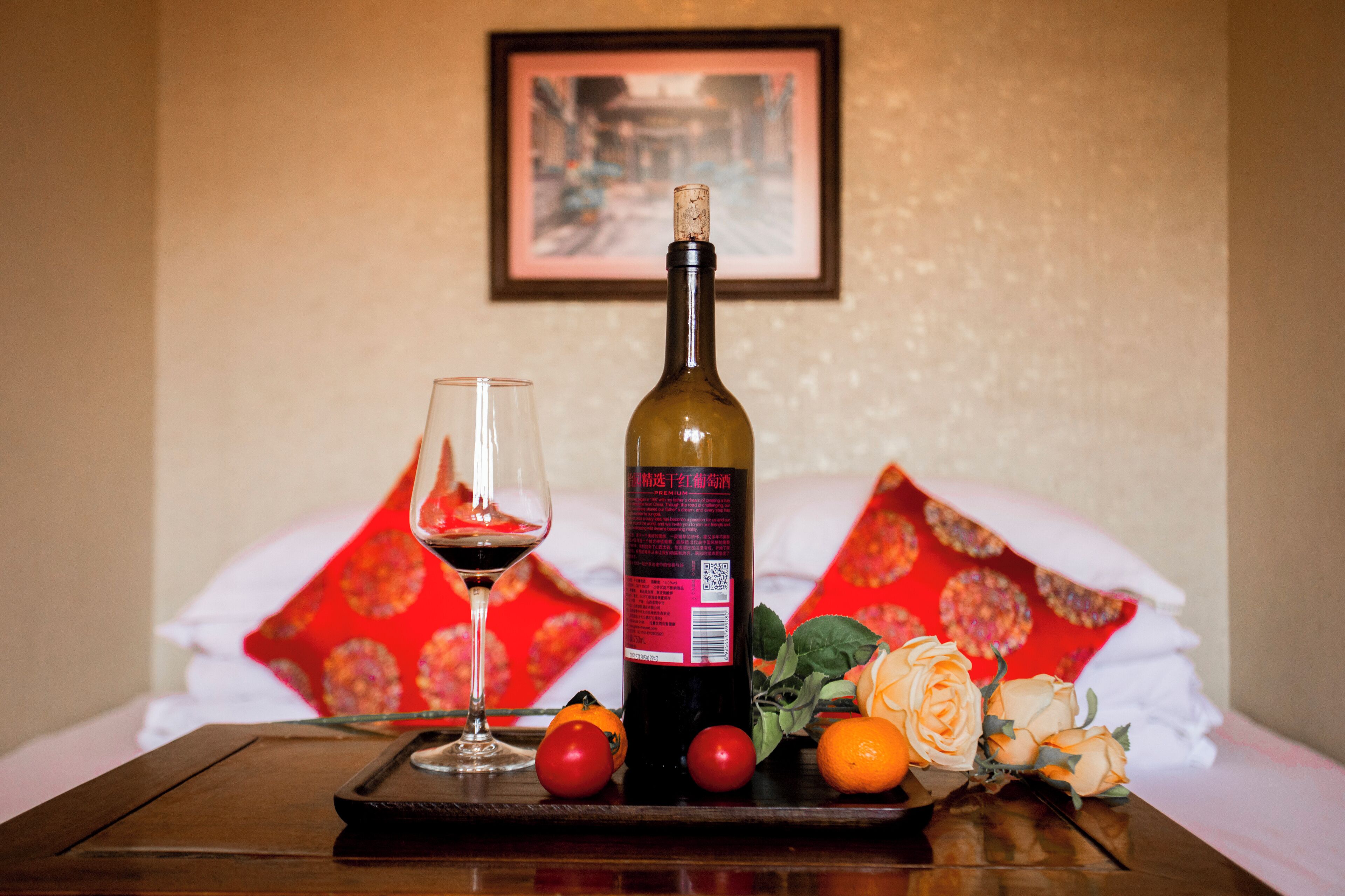 Uma garrafa de vinho, um copo de vinho tinto e algumas frutas em um suporte sobre uma mesa em um quarto de hotel.