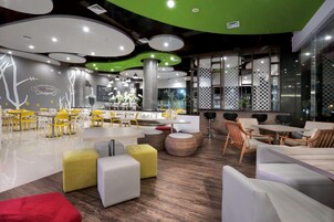 Um hall de hotel moderno com um bar central, áreas de estar e uma parede decorativa.