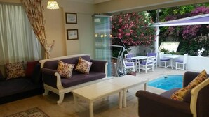 Sala de estar com sofá, mesa de centro e área de piscina com mobiliário ao ar livre.