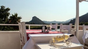 Terraço com mesa posta para dois, com vista para uma paisagem montanhosa.
