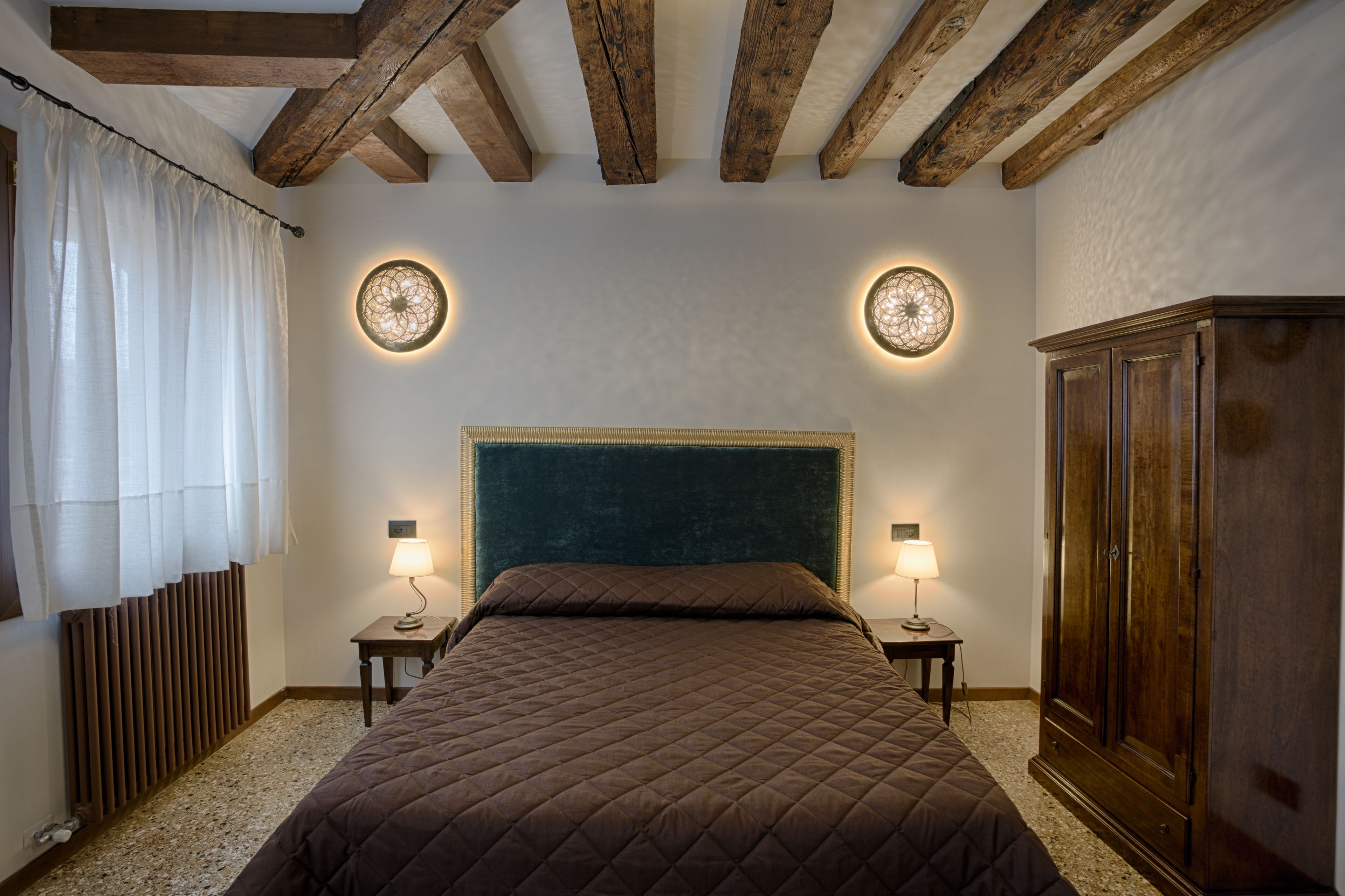 Quarto com uma cama grande, duas mesas de cabeceira com luminárias, um guarda-roupa e teto com vigas de madeira aparente.