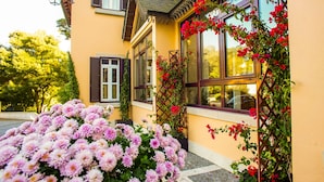 Um edifício com fachada amarela, janelas grandes e uma varanda com flores vermelhas.