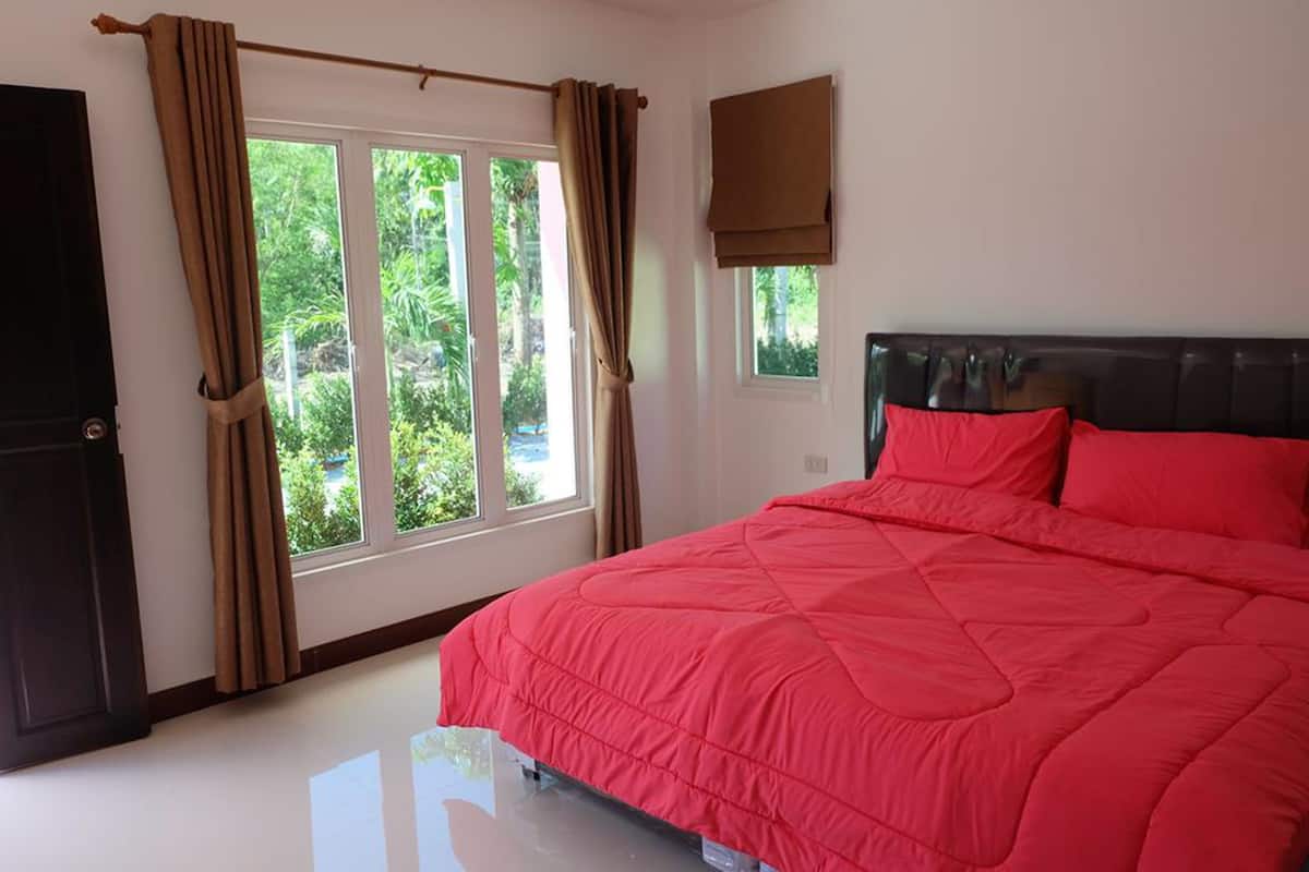 Quarto com uma cama grande, uma janela com cortinas, uma cabeceira escura e uma pequena janela com persiana.