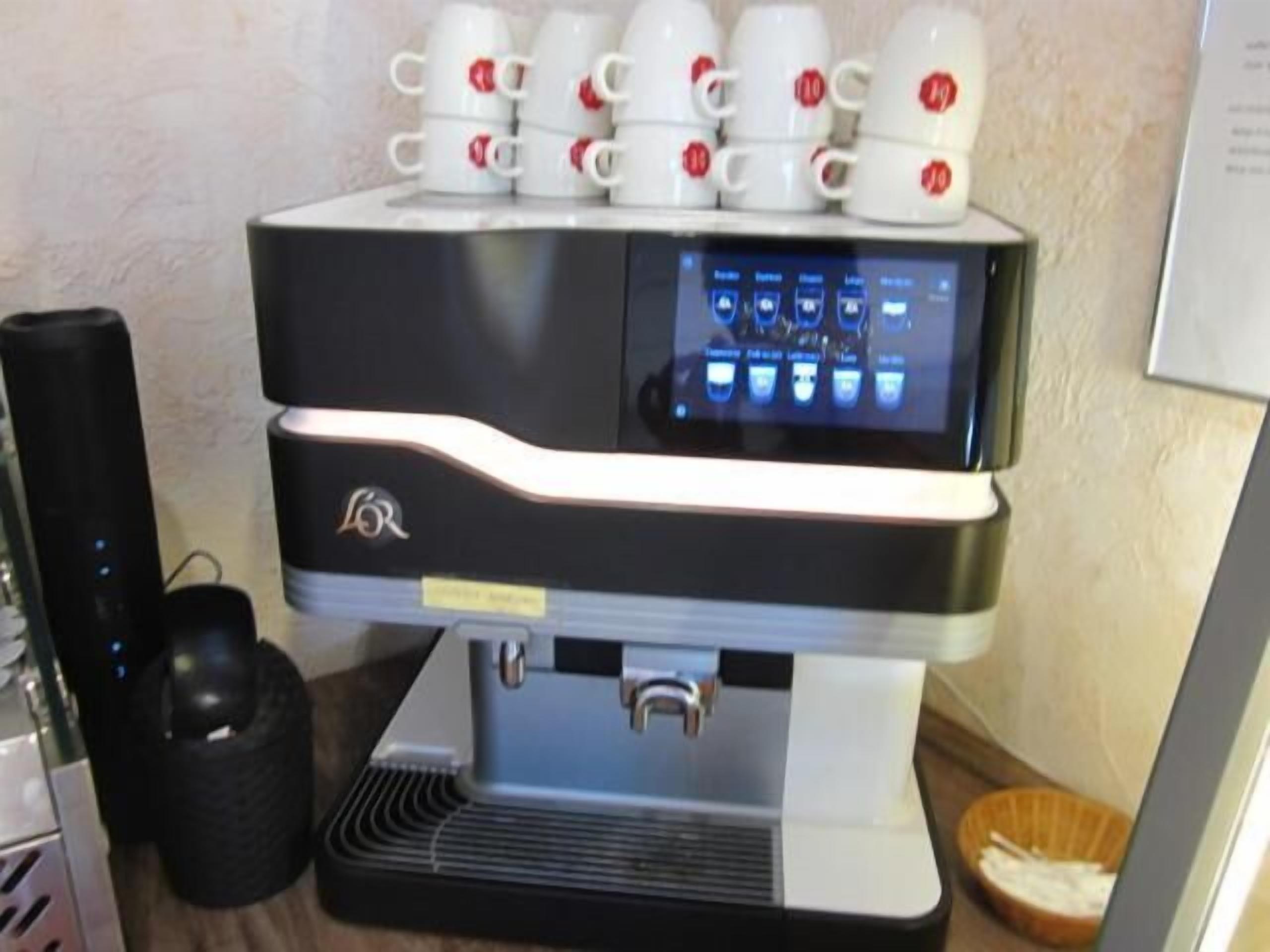 Uma máquina de café com visor digital, uma lixeira e uma cesta.