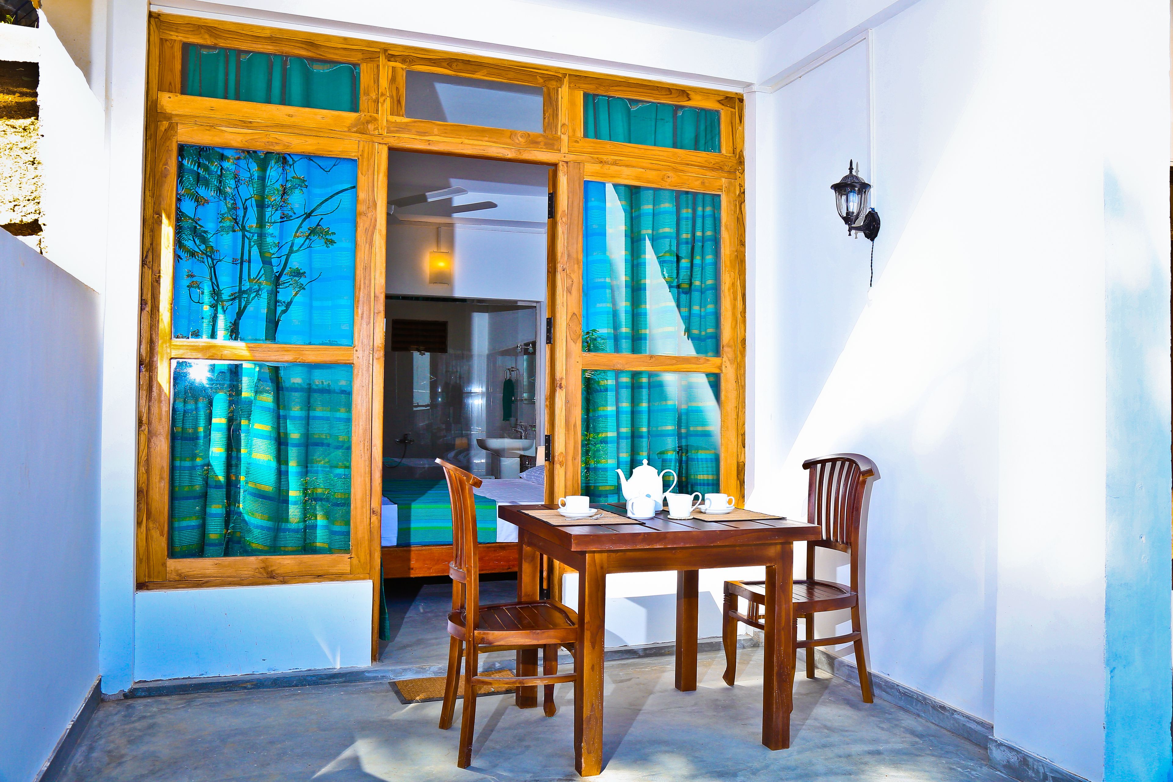 Um quarto com uma mesa e cadeiras de madeira, uma janela com cortinas e um candeeiro fixado na parede.