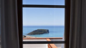Vista da janela com vista para a costa, uma pequena ilha e uma praia.