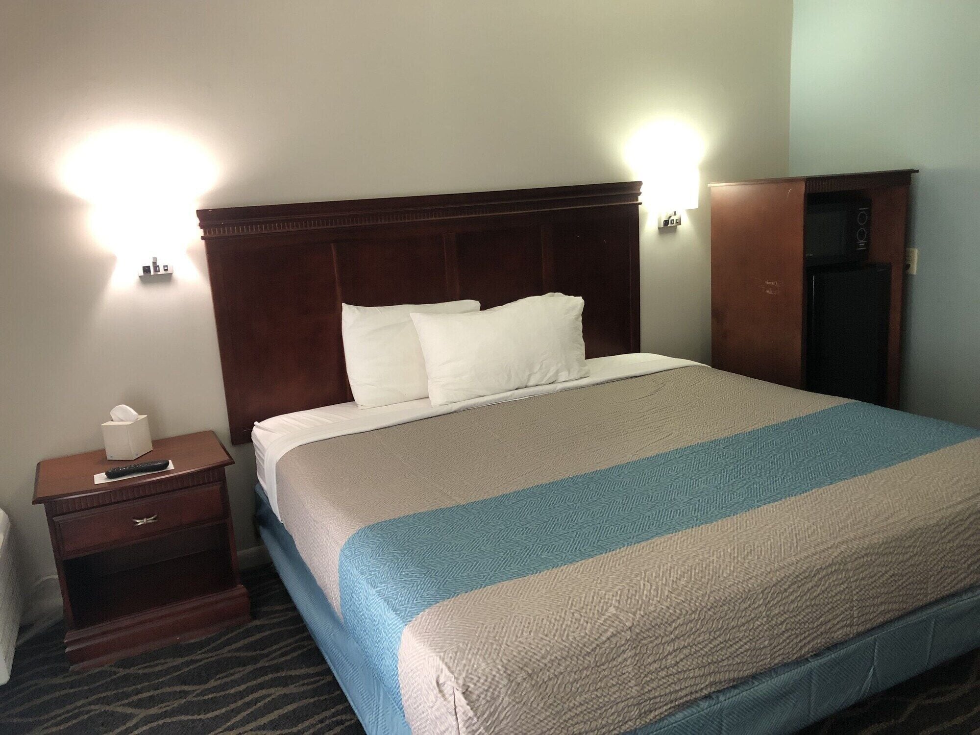 Quarto de hotel com uma cama grande, duas mesinhas de cabeceira, um criado-mudo, uma luminária e uma porta.