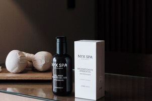 Uma garrafa preta e uma caixa branca com a inscrição NYX SPA em uma superfície refletora.