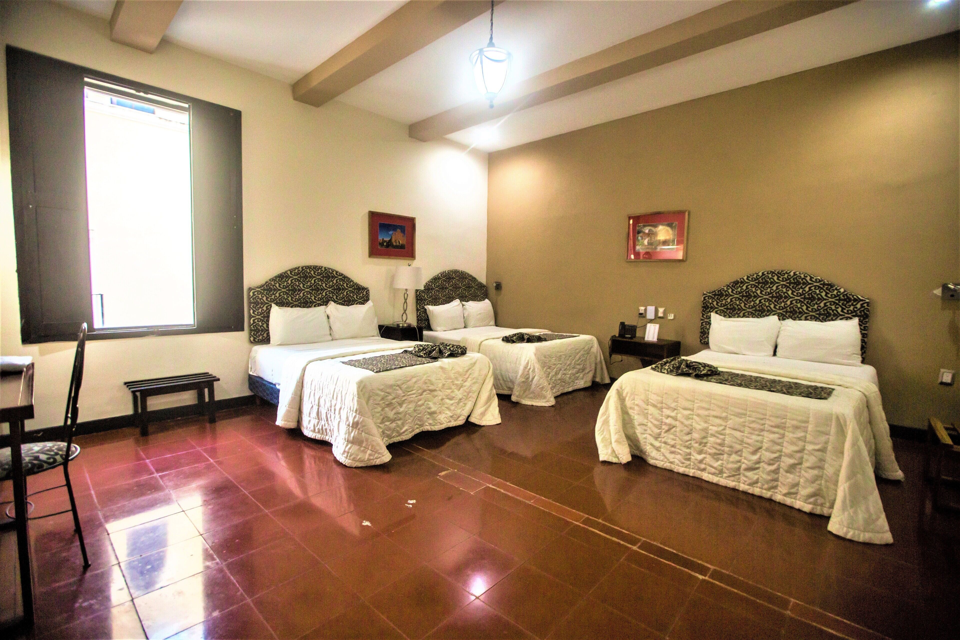 Quarto de hotel com três camas, uma escrivaninha e uma cadeira.