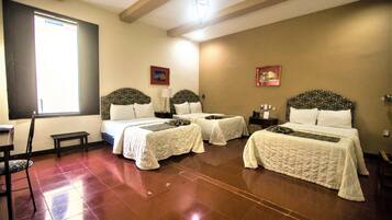 Quarto de hotel com três camas, uma escrivaninha e uma cadeira.