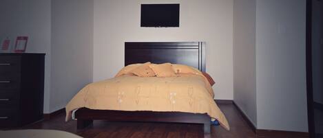Quarto com cama, televisão de tela plana na parede e cômoda de madeira.