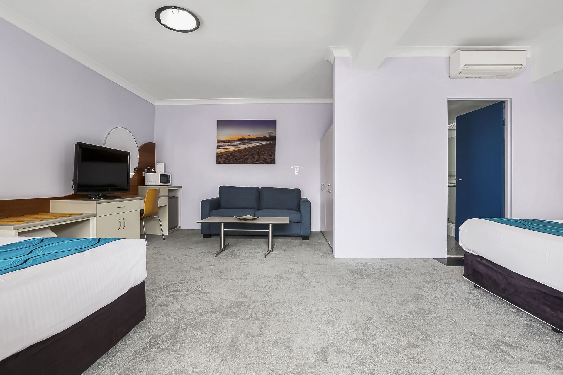 Quarto de hotel com uma cama, uma escrivaninha com computador, um sofá e uma televisão.