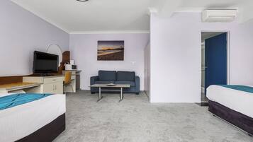 Quarto de hotel com uma cama, uma escrivaninha com computador, um sofá e uma televisão.