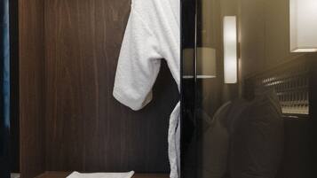 Quarto de hotel com guarda-roupa de madeira, uma toalha branca pendurada na porta, mesa de cabeceira com controle remoto e luminária na parede.