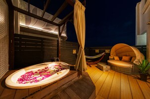 Um deck de madeira com uma banheira de hidromassagem, um espaço de estar acolchoado e uma rede.