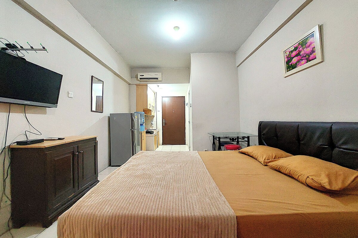 Quarto com cama, televisão na parede, mesa pequena e armário.