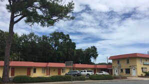 Um motel com teto vermelho, placa de identificação e área de estacionamento com carros.