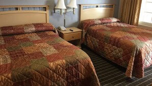 Quarto de hotel com duas camas, cada uma com colcha acolchoada, mesa de cabeceira com abajur e telefone.