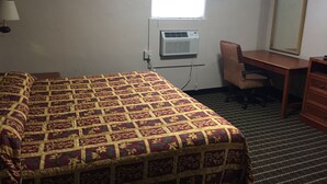 Quarto de hotel com cama, escrivaninha, cadeira, ar condicionado e janela.