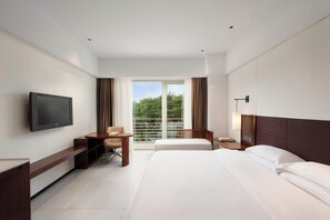 Quarto de hotel com uma cama, uma mesa, uma cadeira, uma televisão e uma janela com cortinas.