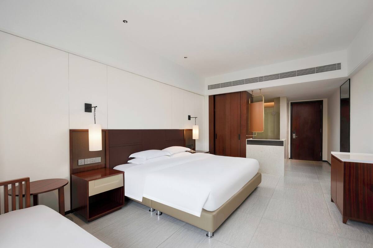 Quarto de hotel moderno com uma cama grande, mesas de cabeceira, escrivaninha, cadeira, guarda-roupa e espelho.