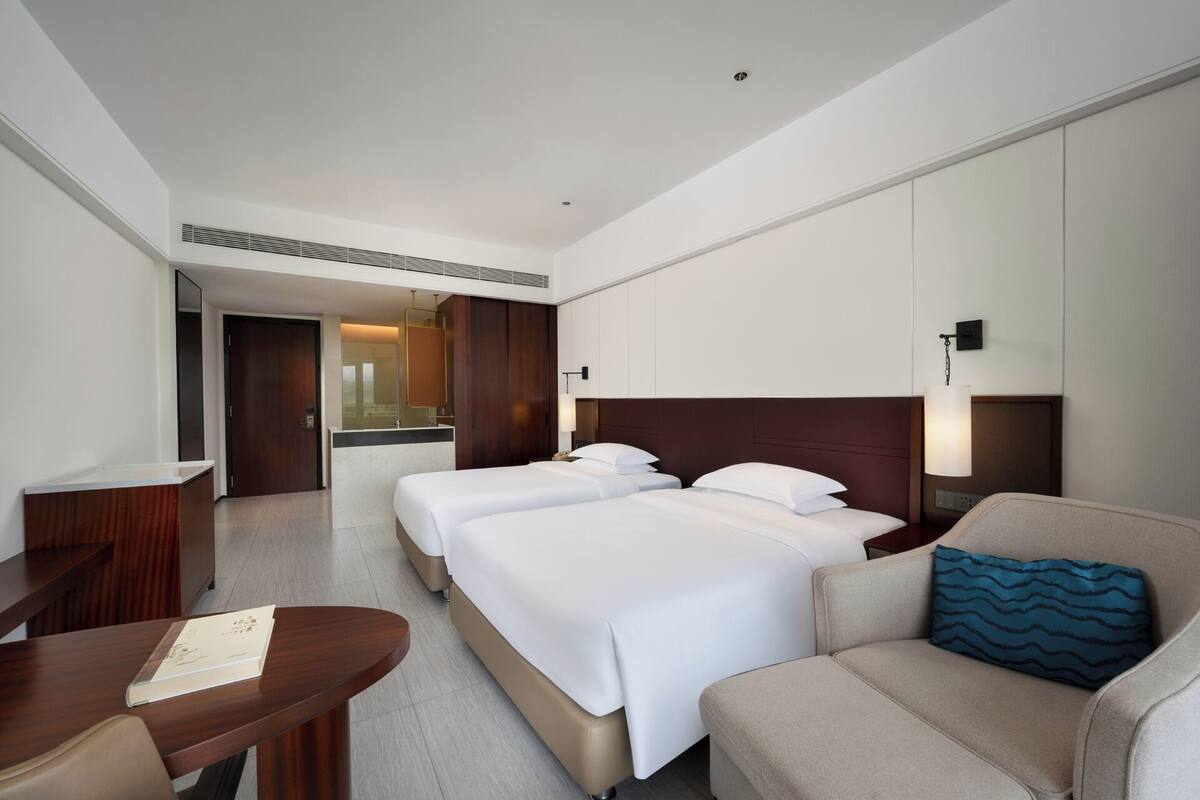 Quarto de hotel com duas camas, uma escrivaninha, uma cadeira e um sofá.