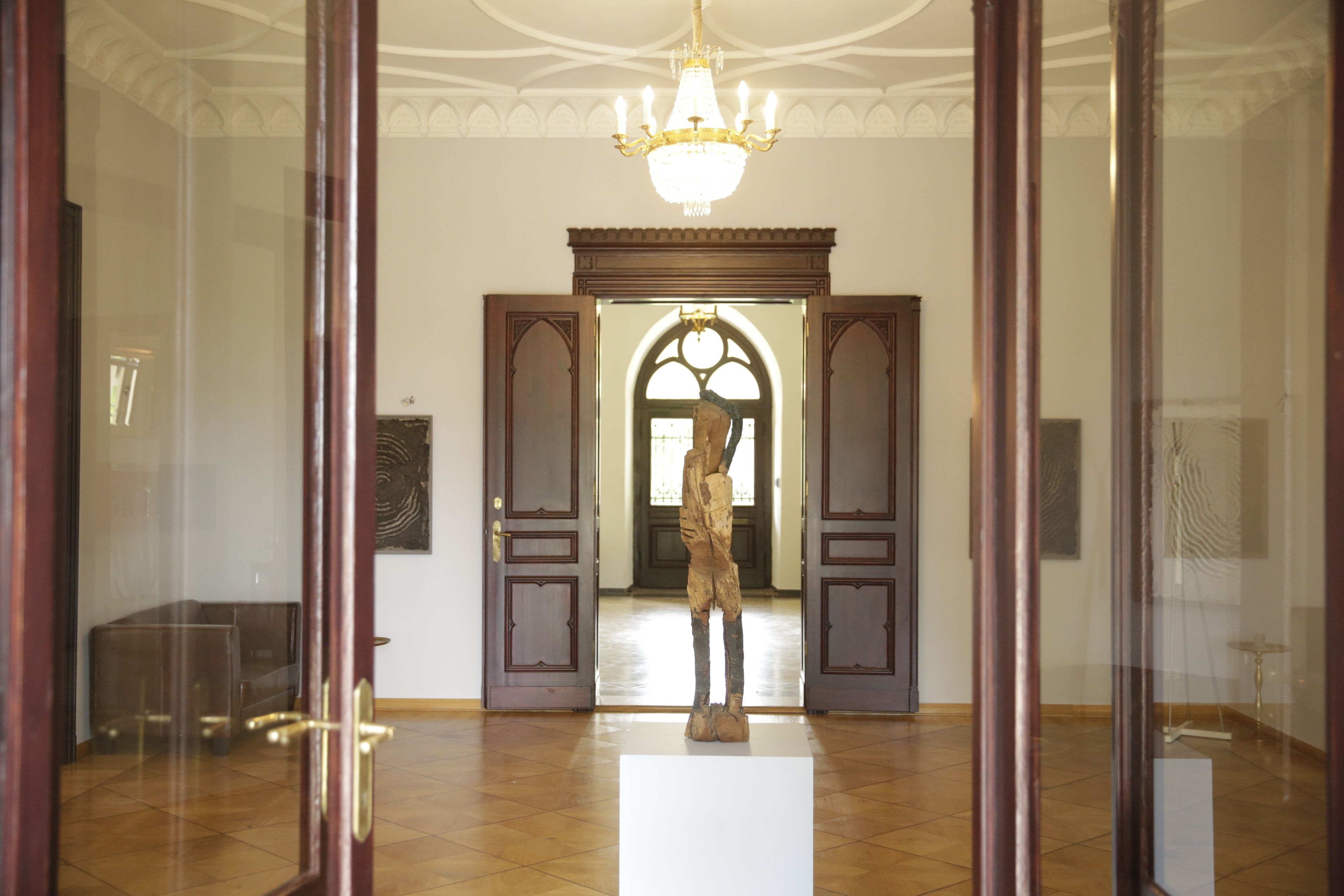 Um hall imponente com um candelabro, portas de madeira e uma estátua.