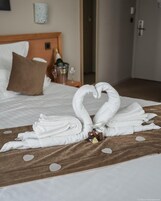 Cama bem arrumada com colcha marrom e recortes em formato de coração, cabeceira de madeira e mesa de cabeceira com uma garrafa e copos.