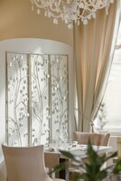 Uma sala de jantar com uma mesa posta para dois, uma parede decorativa com padrão floral e um candelabro.