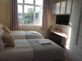 Quarto com duas camas, uma mesa de escritório com computador e janela com cortinas.
