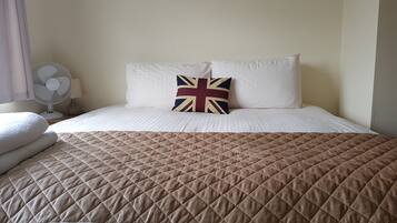 Cama bem arrumada com cobertura marrom acolchoada, almofadas brancas e uma almofada com a bandeira do Reino Unido.