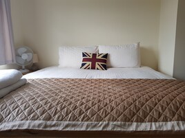 Cama bem arrumada com cobertura marrom acolchoada, almofadas brancas e uma almofada com a bandeira do Reino Unido.