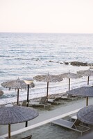Praia com cadeiras de praia e guarda-sóis de palha, com vista para o mar.