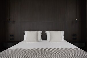 Quarto de hotel moderno com uma cama grande, duas mesas de cabeceira e um tapete estampado.